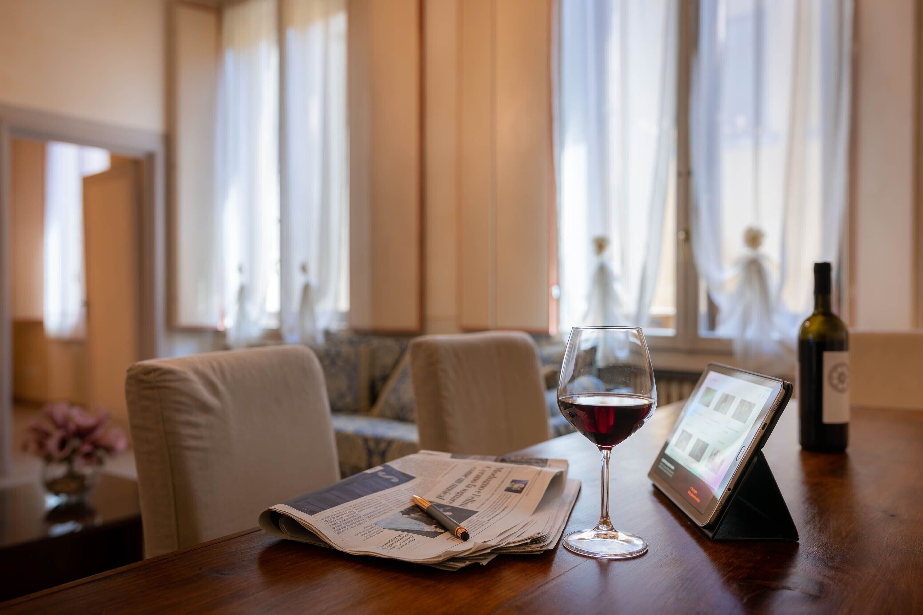 Uma mesa de madeira com um jornal, uma taça de vinho e uma garrafa de vinho.