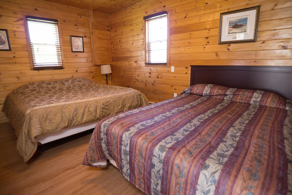 Um quarto no estilo cabana com duas camas, paredes de madeira e quadros emoldurados.