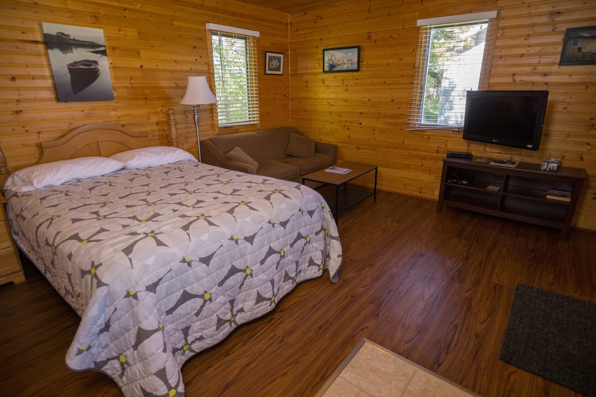 Quarto de cabana de madeira com uma cama, um sofá, uma TV e uma pequena mesa.