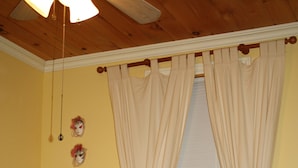 Quarto com cama, cortinas, janela com persianas e detalhes decorativos nas paredes.