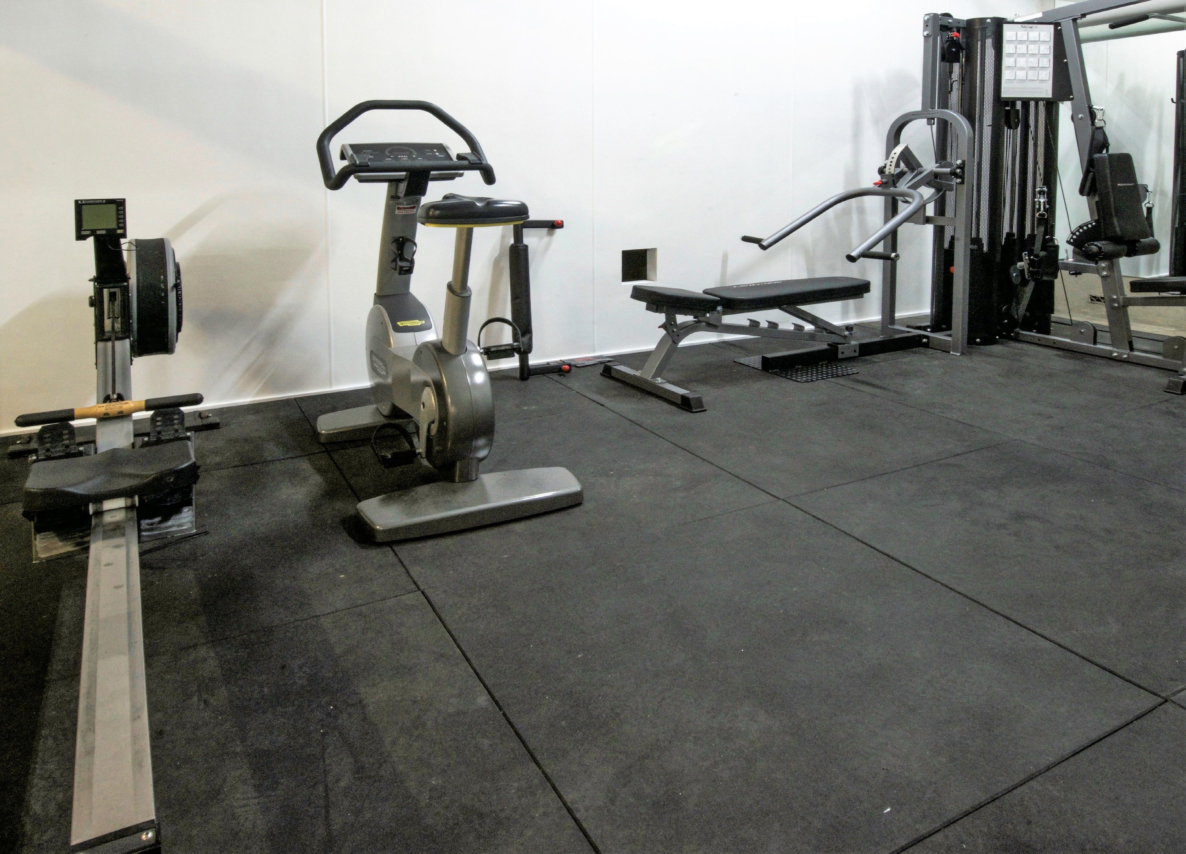 Uma academia com equipamentos de cardio, aparelhos de musculação e um banco.