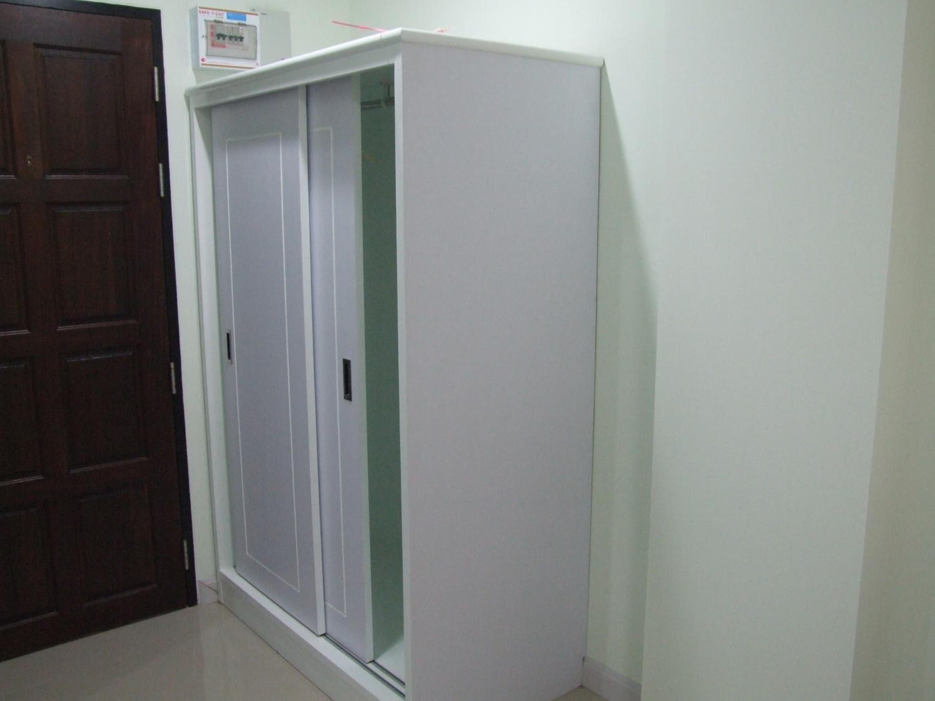 Um guarda-roupa branco com porta interior verde, uma porta de madeira à esquerda e uma parede branca com um sinal de segurança em cima do guarda-roupa.