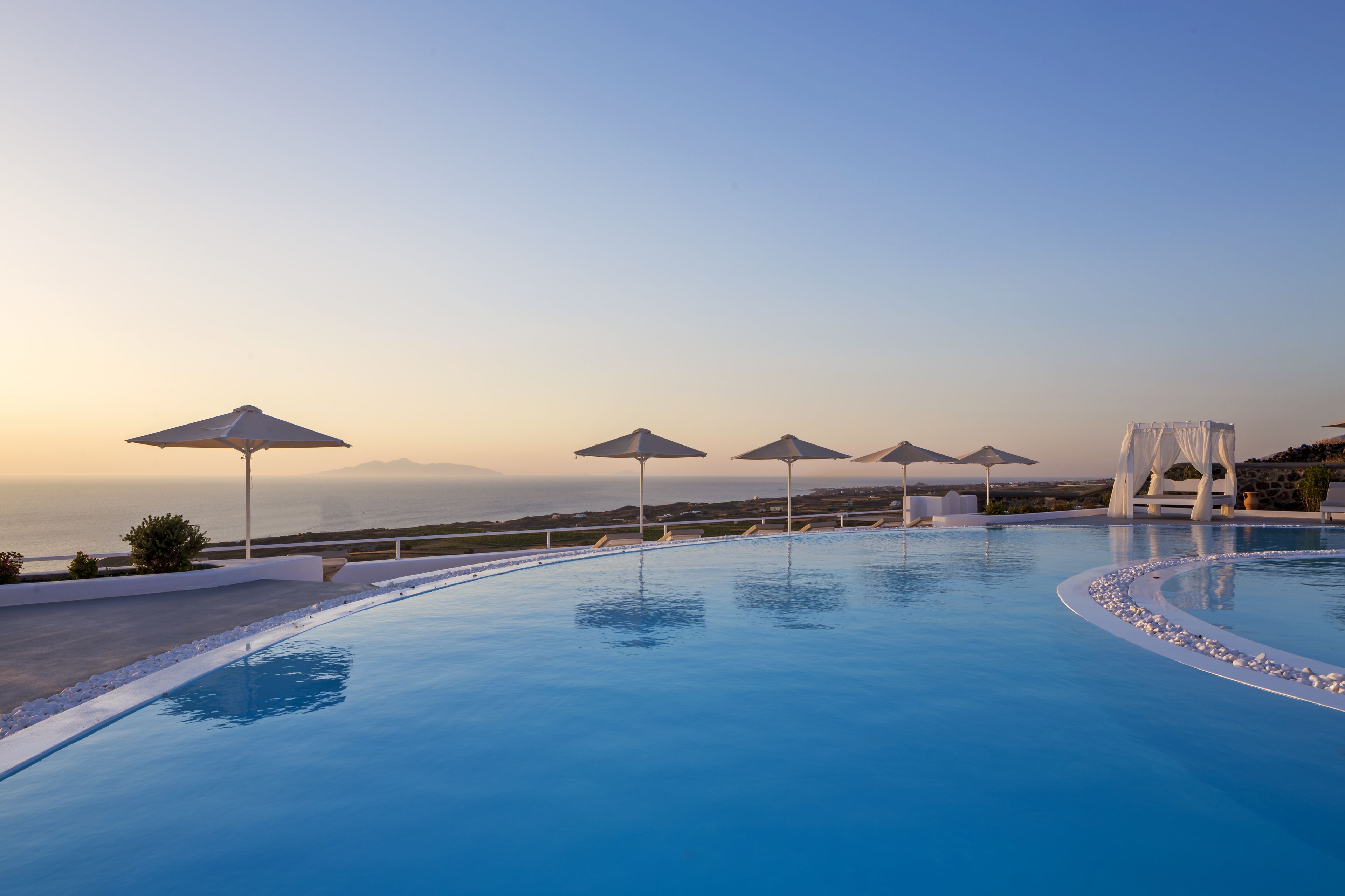 Piscina com guarda-sóis e espreguiçadeiras, céu claro e vista para o mar.