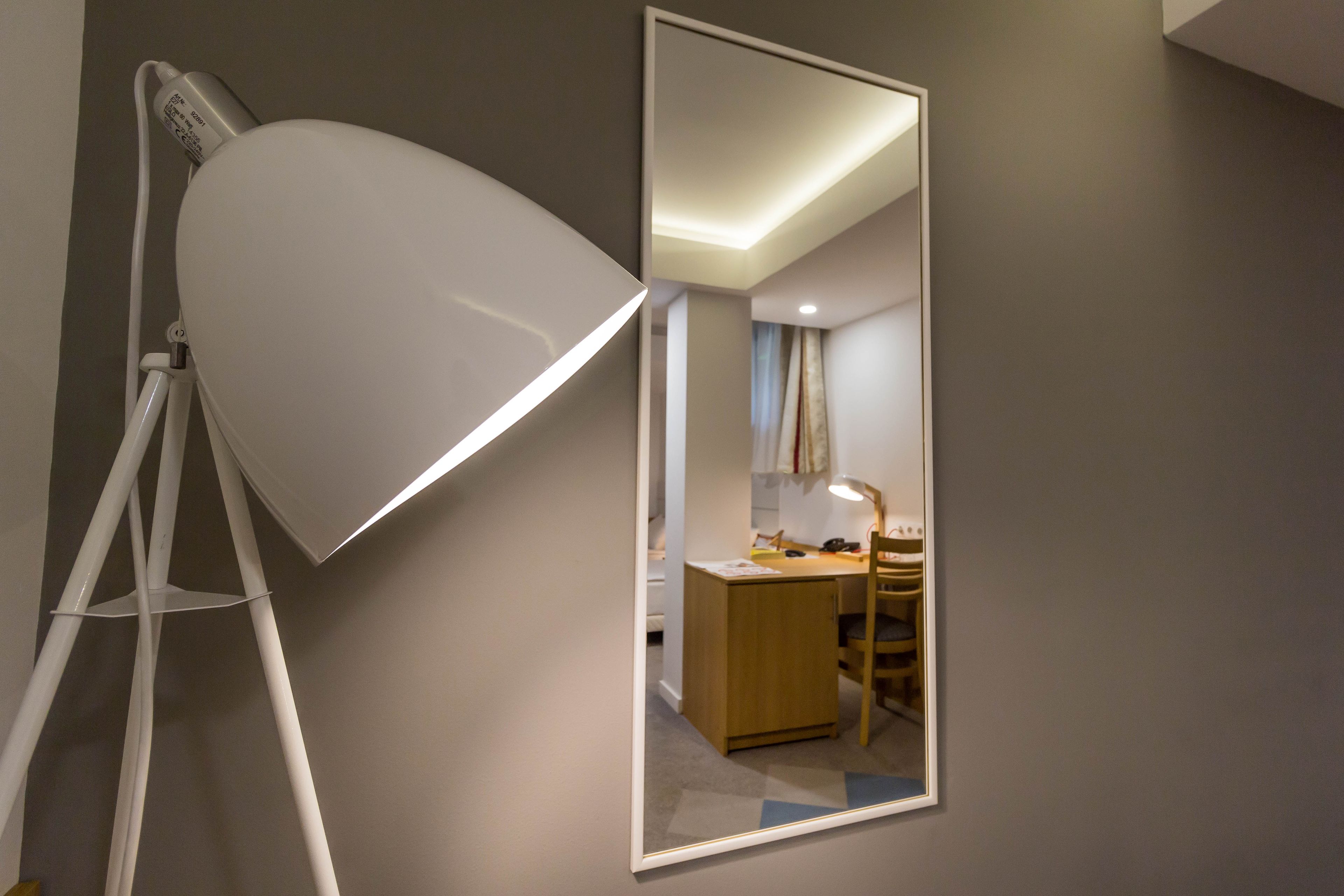 Quarto com escrivaninha, cadeira e um espelho grande refletindo o interior.