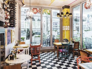 Interior de café com chão quadriculado, mesas, cadeiras e vista para a rua.