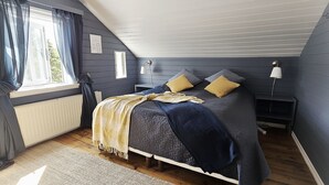 Quarto com cama, mesas de cabeceira, abajur e janela com cortinas.
