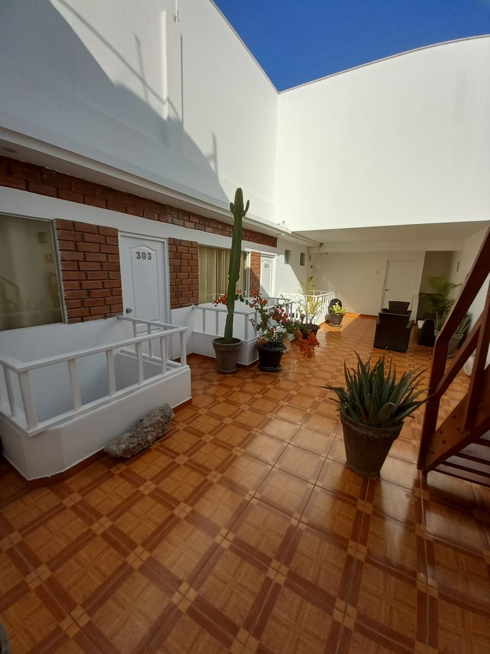 Um pátio com piso de azulejos, plantas em vasos, um banco branco e uma escadaria.