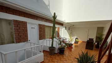 Um pátio com piso de azulejos, plantas em vasos, um banco branco e uma escadaria.