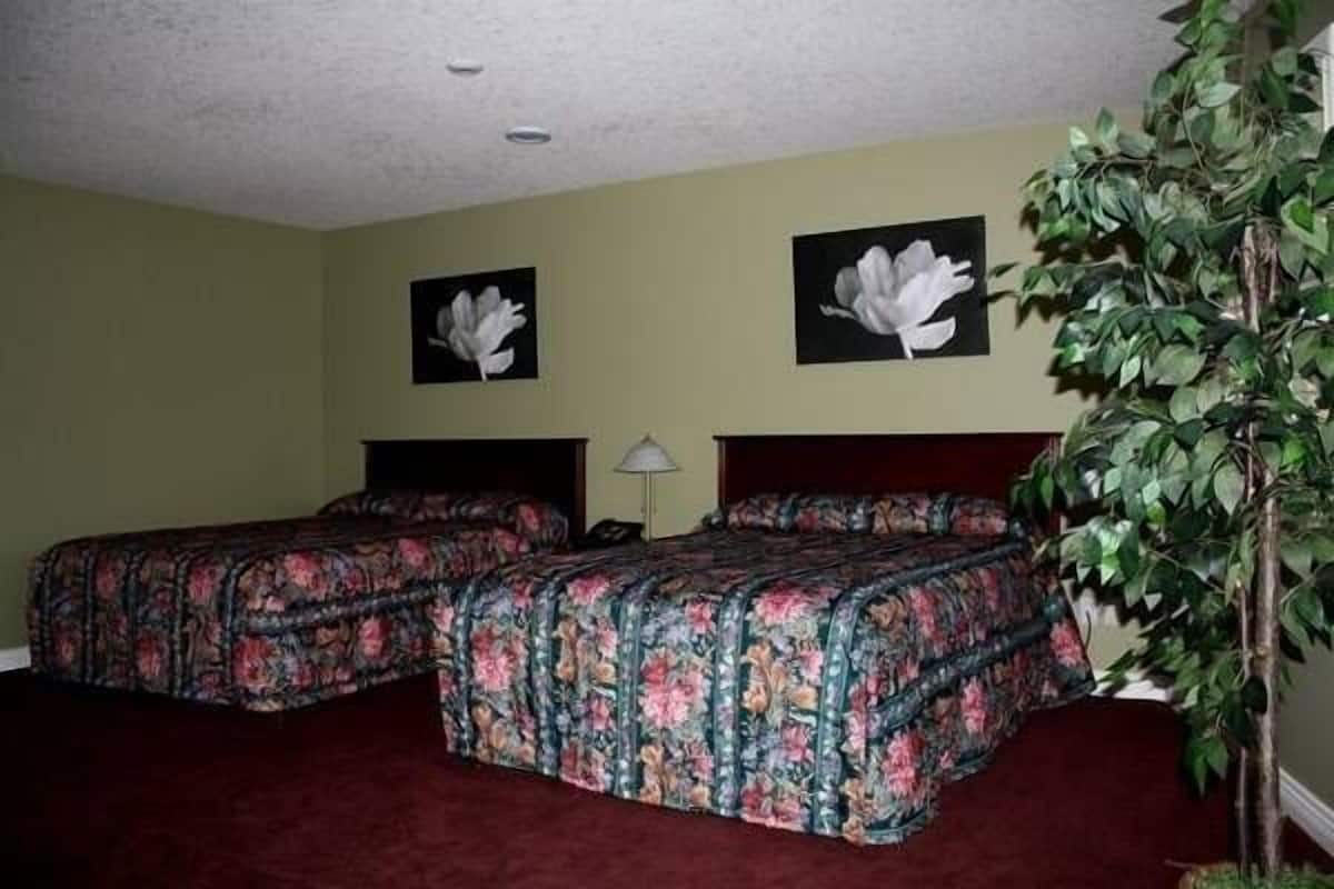 Quarto de hotel com duas camas, roupa de cama com padrão floral, tapete vermelho e duas luminárias fixadas na parede.