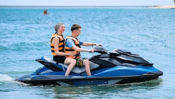 Duas pessoas em um jet ski, com vista para a água e uma linha de costa distante.