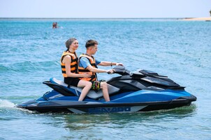 Duas pessoas em um jet ski, com vista para a água e uma linha de costa distante.