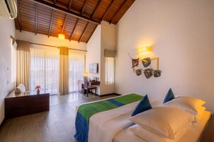 Quarto de hotel com cama, escrivaninha e cadeira, uma janela grande com cortinas e teto com vigas de madeira.
