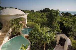 Resort com várias piscinas cercadas por vegetação exuberante e um edifício em formato de cúpula.