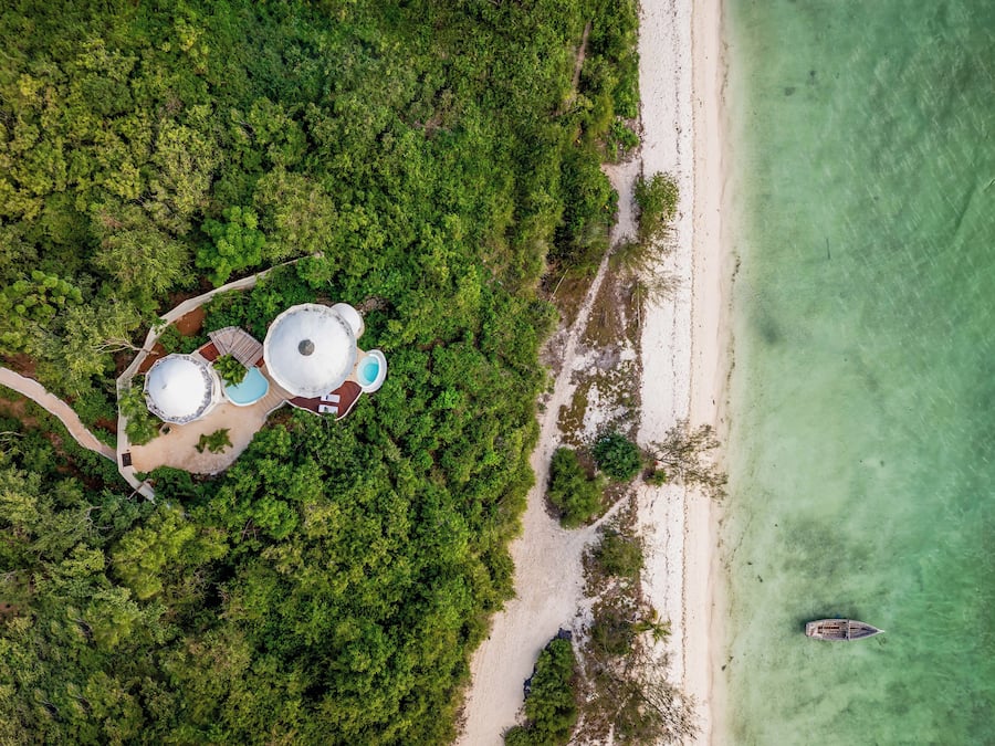 Vista aérea de um resort com várias estruturas, uma praia e um barco.
