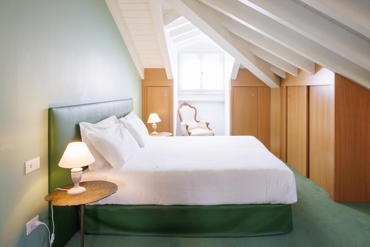 Quarto com cama, luminárias de cabeceira, uma cadeira e painéis de madeira.