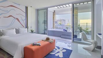 Quarto de hotel moderno com uma cama grande, uma varanda com vista e um espaço de estar com uma cadeira.