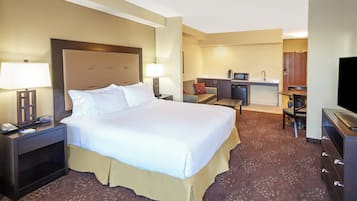 Quarto de hotel com cama grande, escrivaninha, cadeira, televisão e cozinha compacta.