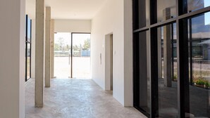 Um corredor com sinalização de direção, janelas amplas e piso de concreto.