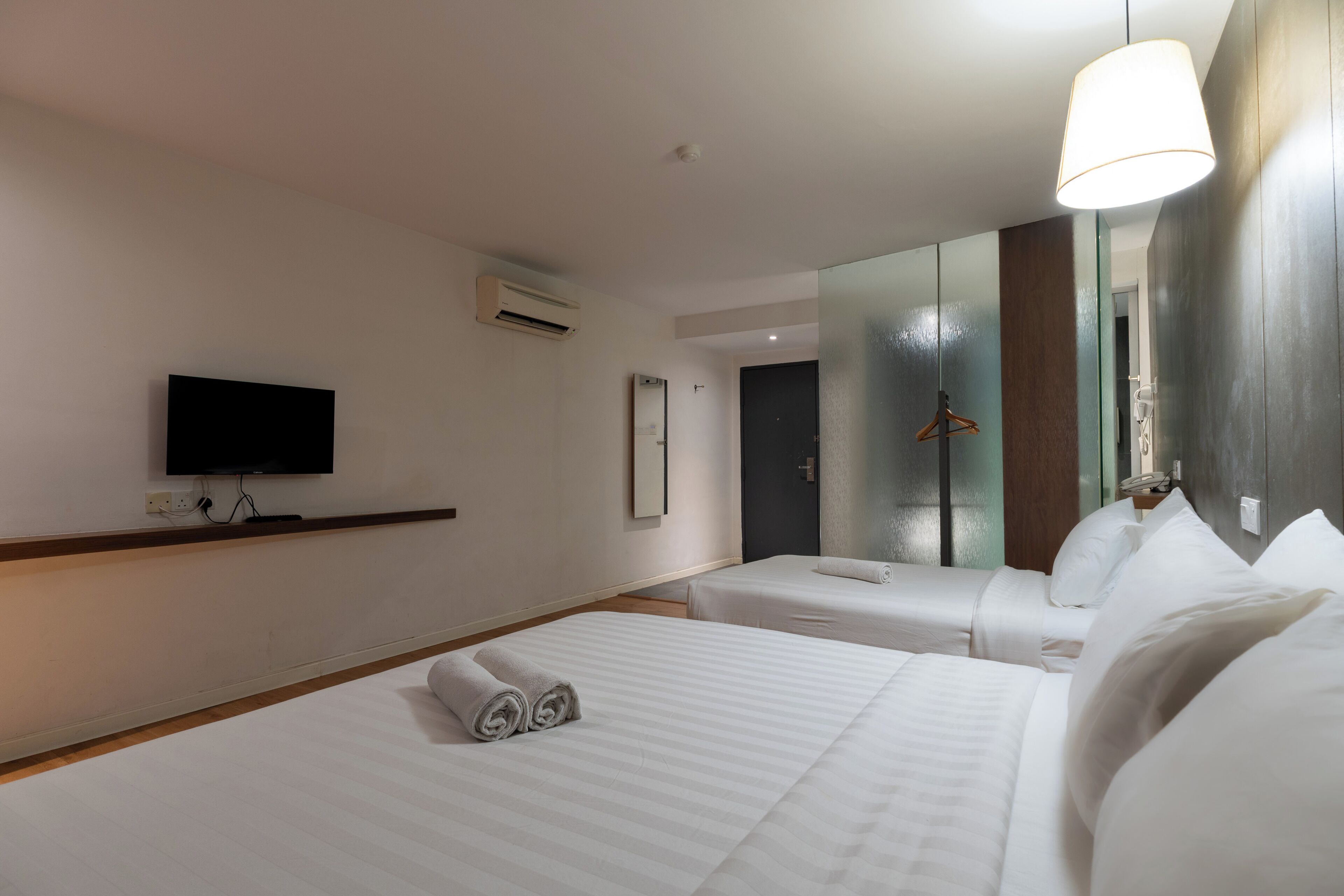 Quarto de hotel com duas camas, uma TV de tela plana na parede, um espelho e um lustre.