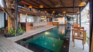 Uma área de piscina com bar, deck de madeira e decoração em bambu.