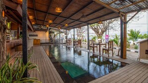 Área de piscina ao ar livre com deck de madeira, espreguiçadeiras e mesas.