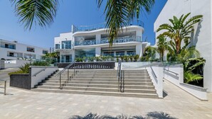 Um edifício moderno com uma escadaria que leva a uma varanda, cercado por palmeiras e vegetação.