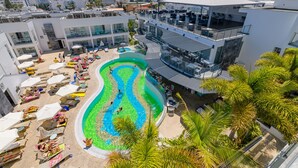 Uma piscina no terraço com design ondulado, rodeada por espreguiçadeiras e guarda-sóis, com vista para a paisagem urbana.
