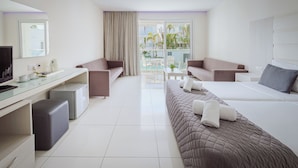 Quarto de hotel moderno com cama, escrivaninha, sofá e varanda com vista para palmeiras.