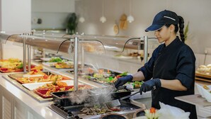 Disposição de buffet com diversos alimentos e uma pessoa servindo.