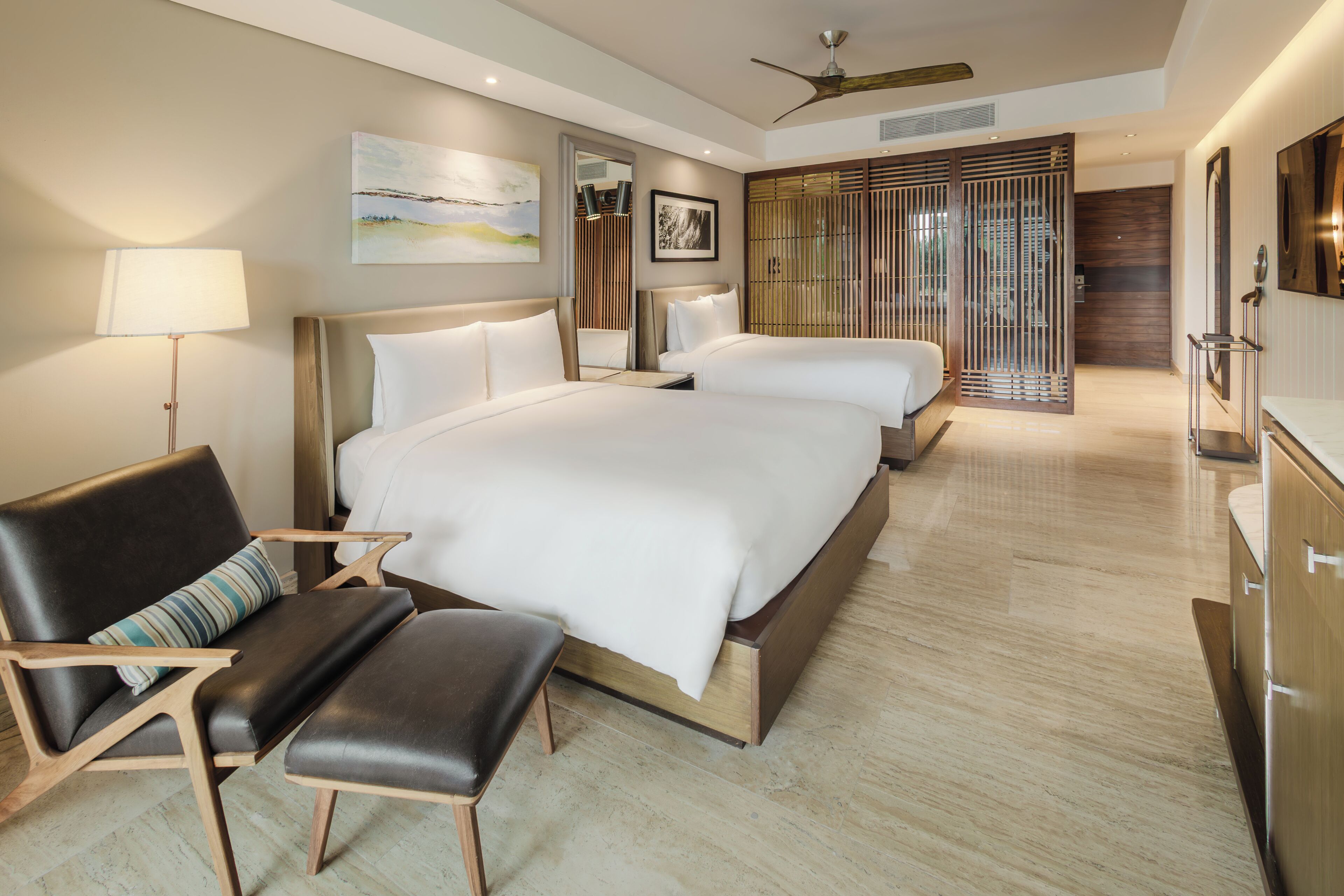 Quarto de hotel com uma cama grande, uma escrivaninha, uma cadeira e um abajur.