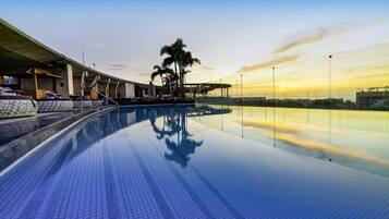 Uma piscina moderna infinita com vista desimpedida para o pôr do sol, palmeiras e uma área de estar coberta.