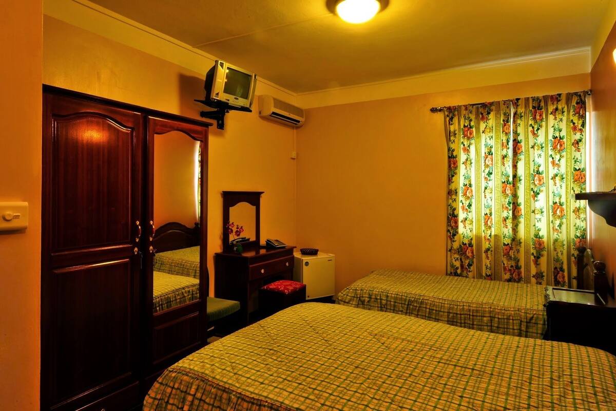 Quarto de hotel com duas camas, um guarda-roupa de madeira, uma pequena mesa de escritório, um espelho e uma televisão.