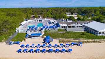 Vista aérea de um resort com piscina, área de praia com guarda-sóis e um edifício grande com terraço coberto.