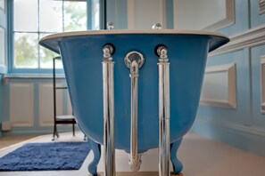 Uma banheira de pés de leão azul com detalhes cromados em um quarto com paredes azuis e uma janela.