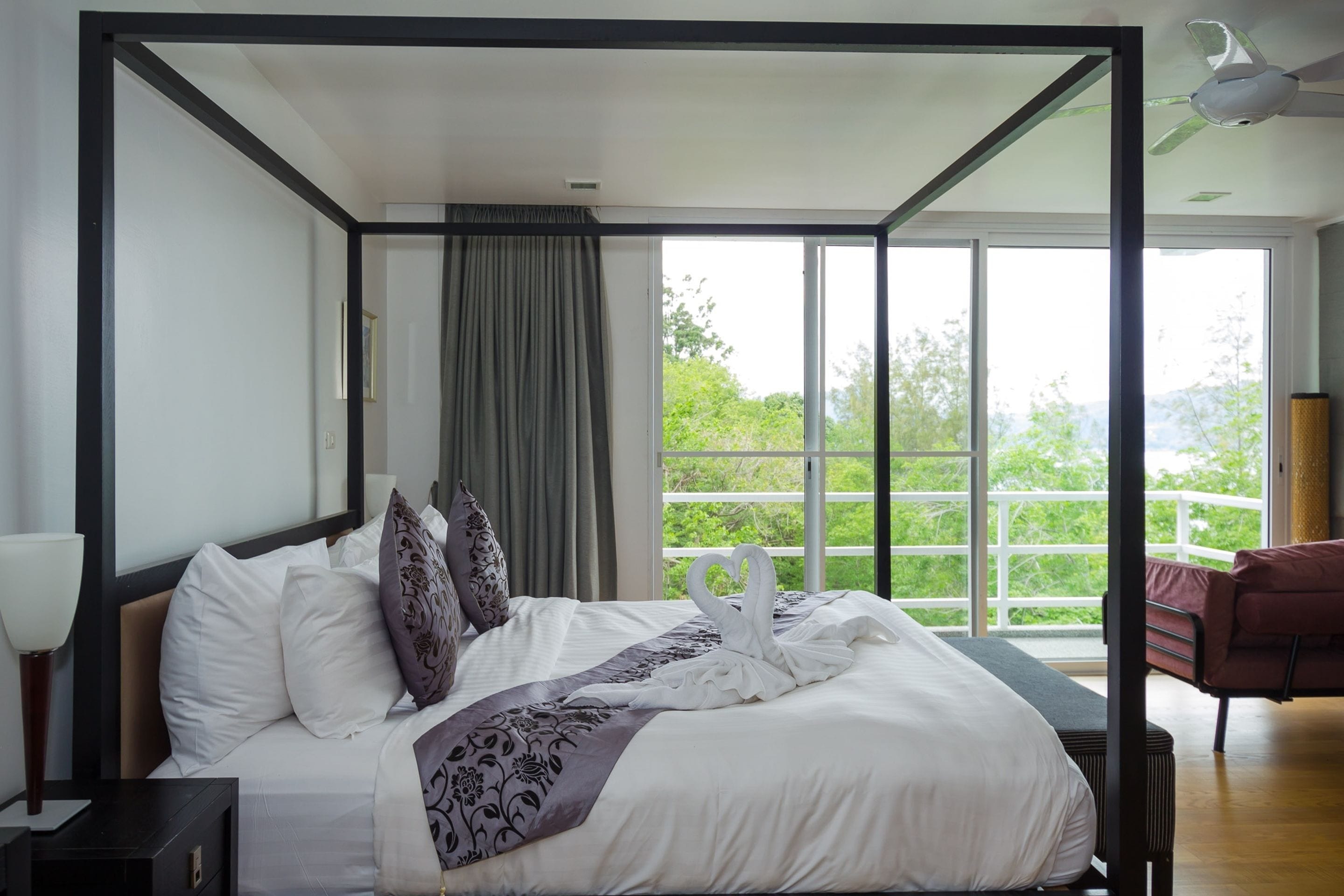 Quarto moderno com cama de dossel, vista para o verde através de grandes janelas e um ventilador de teto.