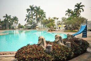 Piscina com um atrativo aquático, palmeiras e um escorrega.