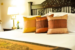 Cama com cabeceira de madeira e três almofadas em tons de amarelo e castanho.