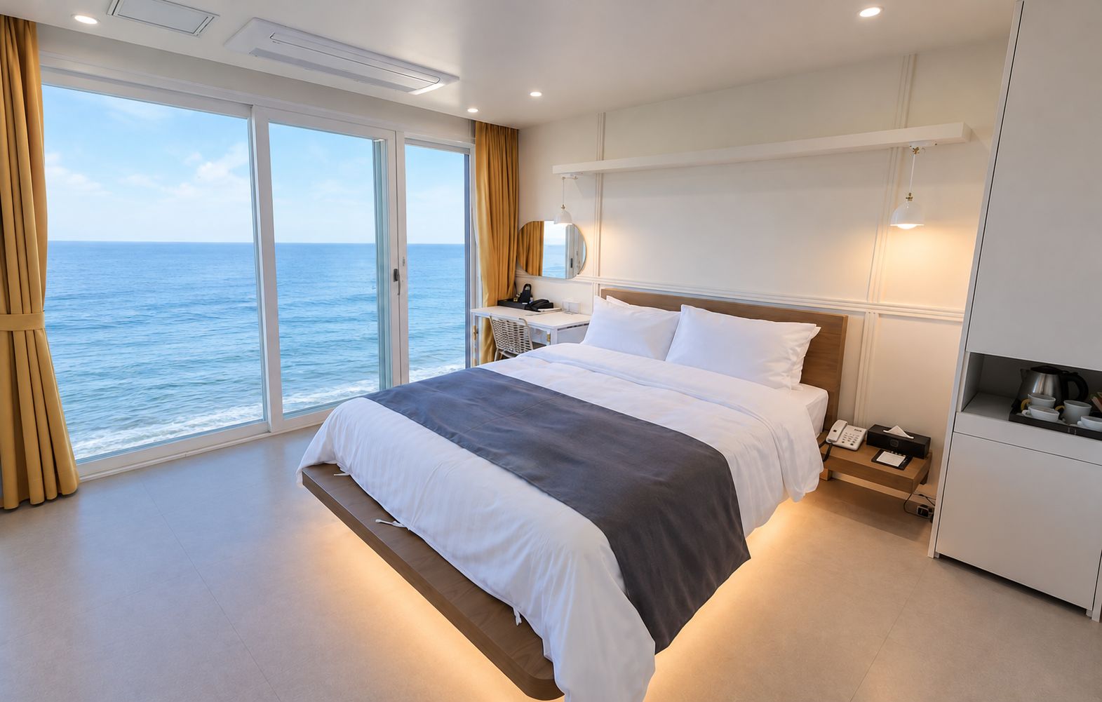 Quarto de hotel com uma cama grande, uma escrivaninha, uma cadeira, uma mesa de cabeceira, um telefone e uma prateleira com chaleira e chávenas.