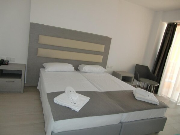 Quarto de hotel com uma cama grande, mesas de cabeceira, uma cadeira e uma janela com cortinas.