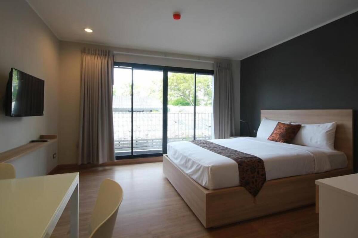Quarto de hotel com cama, televisão, escrivaninha e varanda com vista.