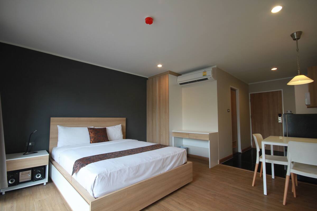 Quarto de hotel moderno com uma cama grande, mesa de cabeceira e uma pequena área de trabalho com uma cadeira.