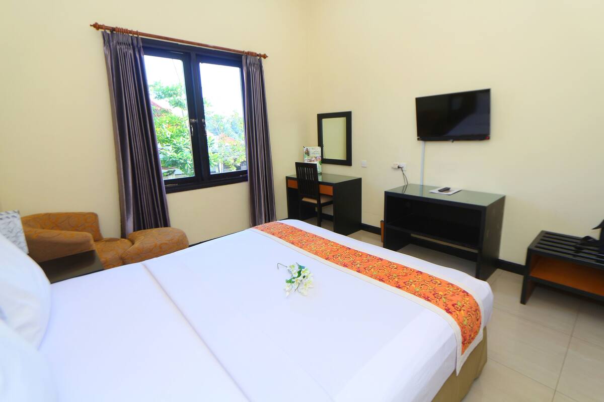 Quarto de hotel com cama, escrivaninha, cadeira, televisão e janela com cortinas.