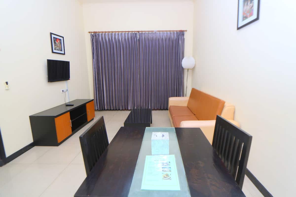 Uma sala de estar pequena e moderna, com uma mesa de madeira escura, um sofá e uma televisão fixada na parede.