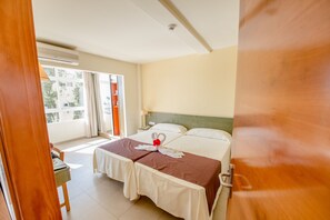 Quarto de hotel com cama, escrivaninha e janela com vista para edifícios.