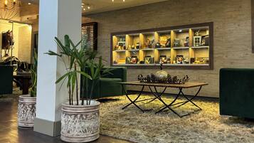 Um hall moderno com piso de madeira, um sofá verde, uma mesa com objetos decorativos e uma parede com prateleiras exibindo diversos itens.
