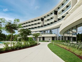 Um edifício moderno com fachada curva, várias varandas e um jardim bem cuidado com caminhos.