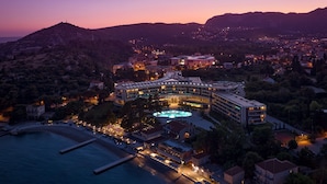 Vista aérea de um hotel à beira-mar, com piscina, vários edifícios e uma área de praia.