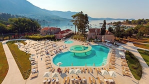 Um resort com uma piscina grande, espreguiçadeiras e vista para o mar e montanhas.