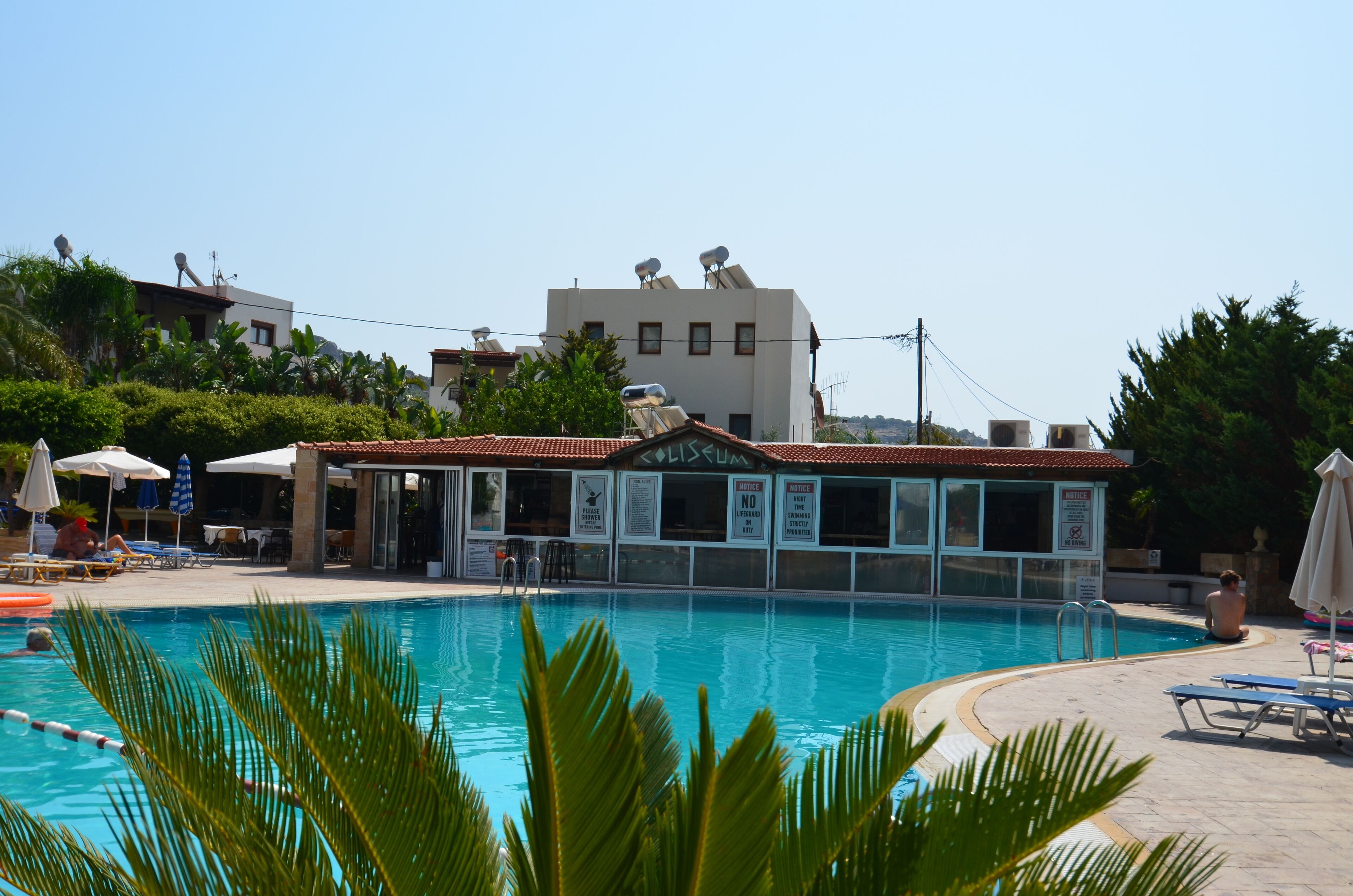 Uma área de piscina com espreguiçadeiras, guarda-sóis e um edifício com placas.