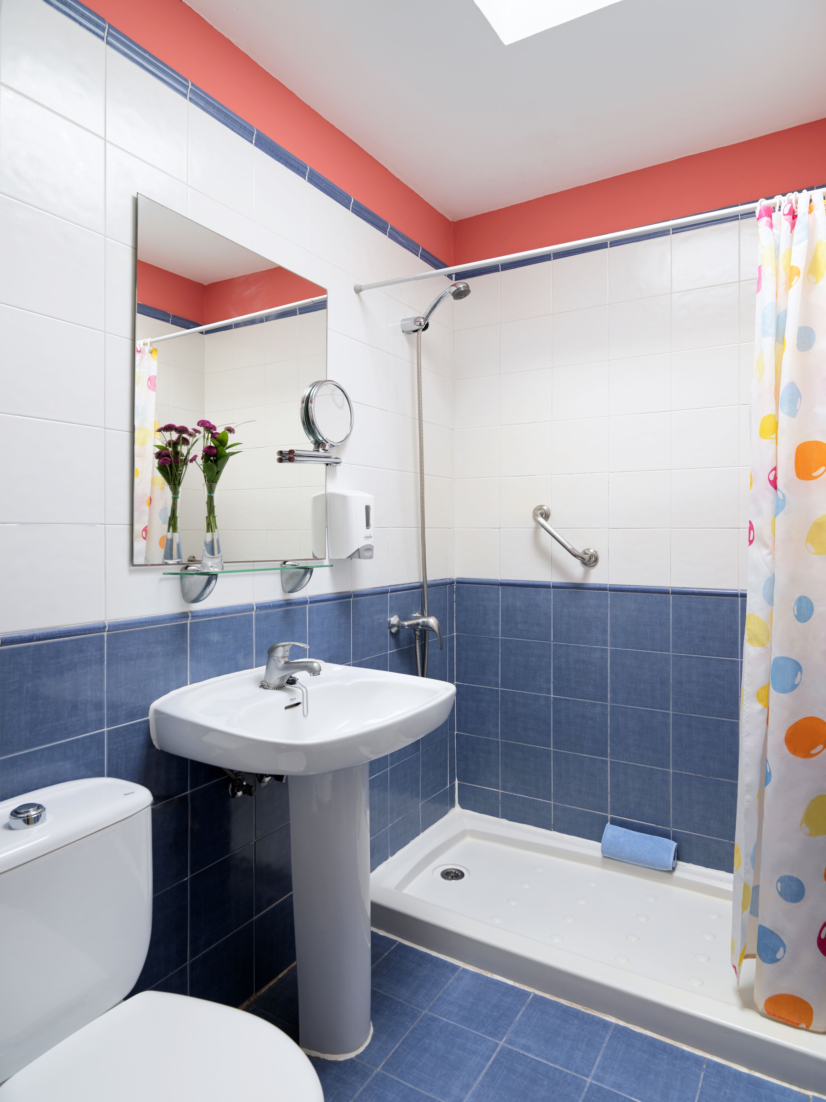 Uma casa de banho com uma pia branca, um espelho, um chuveiro com cortina colorida e azulejos azuis e brancos.